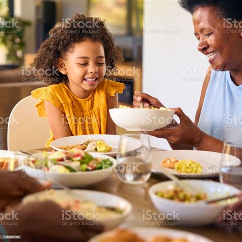 Multigeneration Family Sitting Around Table Serving Food For Meal At Home Stock Photo - Download ...
