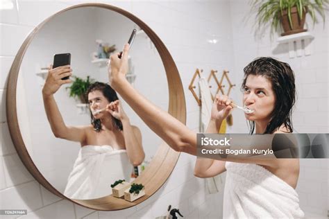 소셜 미디어에 영향을 양치질 하 고 둥근 거울에 세련 된 욕실에 전화 보고 하는 동안 Selfie를 만드는 흰 수건에 젊은 행복 한 여자 자연 피부와 슬림 섹시 한 여자