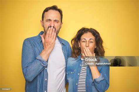 아름 다운 중년 부부 함께 데님 셔츠를 입고 고립 된 노란색 배경 지루한 하품 하품 피곤 한 손으로 입을 덮는 불안과 졸음 2