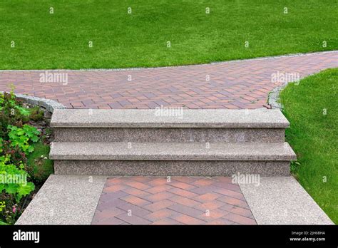 Granite Steps On A Slope Along A Pavement Of Stone Tiles Surrounded By A Landscape With A Green