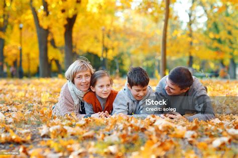 가을 도시 공원에서 놀고 즐기는 낙엽에 누워있는 행복한 가족 아이들과 부모가 함께 좋은 하루를 보내고 나무에 밝은 햇빛과 노란색 잎 가을 시즌 4 명에 대한 스톡 사진 및