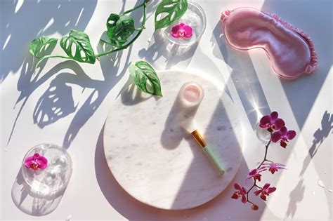 대리석 접시에 보습 크림과 핑크 실크 슬립 마스크 몬스터 나뭇잎과 활기찬 마젠타 난초 꽃이국적인 플랫 누워 햇빛 긴 그림자 얼굴 마사지 배경 복사 공간 눈가리개 안경류에