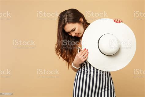 검은 색과 흰색 줄무늬 드레스 지주 모자 파스텔 베이 지 벽 배경에 고립 된 찾고 아름 다운 젊은 여자의 초상화 사람들은 진심으로 감정 라이프 스타일 개념입니다 복사 공간을