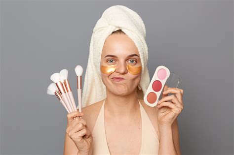 눈꺼풀에 그림자를 드리우고 회색 배경 위에 고립되어 있고 화장을 하고 혼란스러운 표정을 짓고 있는 아름다운 여성의 실내 사진은