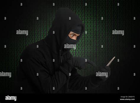 Portrait Of Mysterious Man Wearing Black Hoodie And Mask Doing Hacking Activity On Mobile Phone