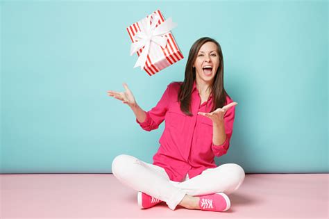 전체 길이 세로 여자 흰 장미 셔츠 블라우스에 밝은 핑크 블루 파스텔 벽 배경 스튜디오에 절연 층 보류 현재 상자에 앉아 바지 패션 라이프 스타일 개념입니다 복사 공간을