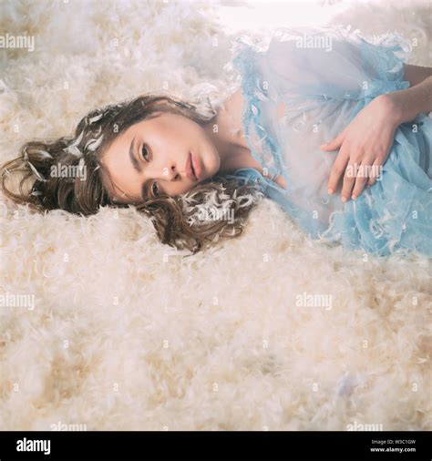 Beautiful Girl Lying On Bed In Middle Of Feathers And Looking At Camera