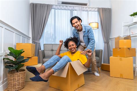 새 아파트로 이사하는 동안 바닥에 앉아서 상자를 풀고 포옹하는 것에 만족하는 젊은 부부 남성과 여성 25 29세에 대한 스톡