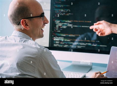 Programmer Working Behind The Desk Analysing Code While Chatting With