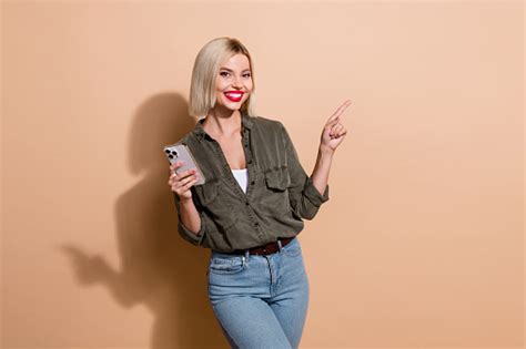 예쁜 달콤한 아가씨 입고 카키색 셔츠 채팅 현대 장치 가리키는 손가락 빈 공간 고립 베이지 색 배경의 사진 Brand Name Smart Phone에 대한 스톡 사진 및