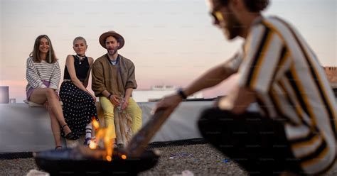 벽난로 근처에 앉아 해질녘에 옥상 테라스에서 함께 어울리는 젊고 세련된 친구들 여름과 아름다운 일몰 전망을 즐기세요 사진 Unsplash의 우크라이나 이미지