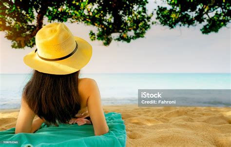 분홍색 수영복과 밀 짚 모자에 행복 한 젊은 아시아 여자의 다시 보기 나무 아래 열 대 모래 해변에서 휴식과 휴가를 즐길 수 있습니다 여름 휴가 패션에 여자입니다 아름다움