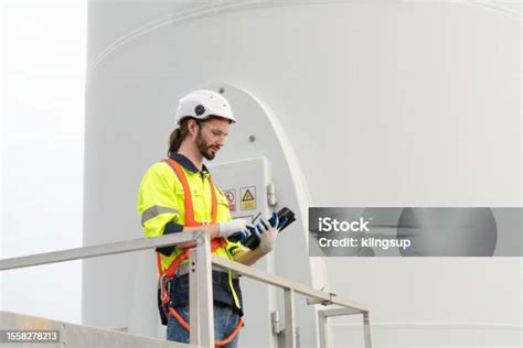 남성 엔지니어 풍차는 태블릿 검사를 사용하여 유니폼과 헬멧을 착용하고 풍력 발전 단지의 풍력 터빈을 점검하여 전기 에너지 재생 에너지를 생성합니다 공학에 대한 스톡 사진 및