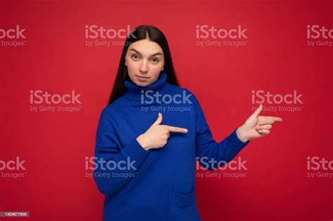 손으로 여유 공간을 가리키는 복사 공간과 배경 벽에 고립 된 캐주얼 의상을 입은 귀여운 멋진 멋진 성인 여성의 사진 스웨터에