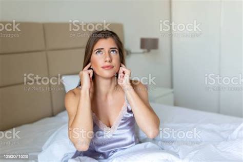 화가 난 젊은 여성은 시끄러운 이웃들에게 고통 받고 방해를 받고 이른 아침에 집에서 침대에서 잠을 자려고 노력하면서 손가락으로 귀를 가렸다 감정에 대한 스톡 사진 및 기타