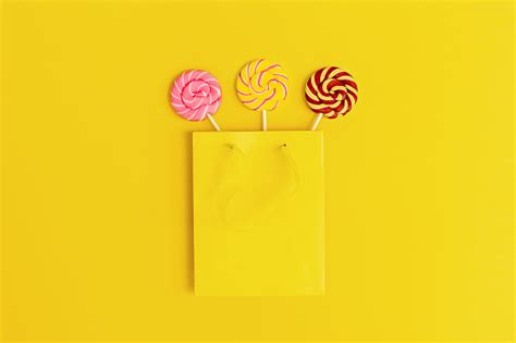 노란색 종이 가방에 막대기에 줄무늬 패턴이있는 3 개의 과자 둥근 사탕 롤리팝 인사말 카드 또는 휴일 개념에 대한 추세 최소한의 스타일 이미지 플랫 레이 3가지 개체에 대한