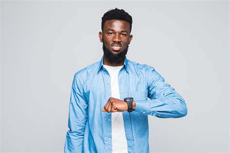 몇 시예요 행복한 얼굴 표정으로 손 시계를 가리키는 흰색 티셔츠와 빨간 셔츠에 어두운 아프로 헤어 스타일을 가진 젊은 매력적인 남자의 초상화 T 셔츠에 대한 스톡 사진 및