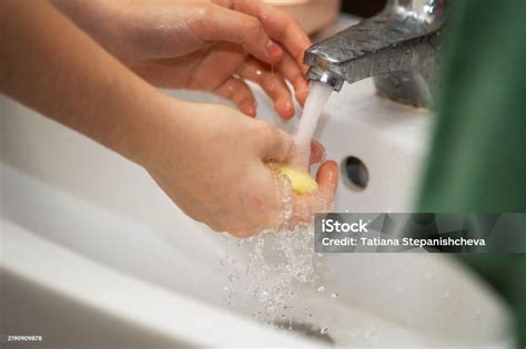 아이는 흐르는 수도꼭지에서 노란 비누를 사용하여 즐겁게 손을 씻습니다 밝은 장면은 위생과 순수의 중요성을 강조하며 장난기 넘치는 청결의 순간을 포착합니다 가정 생활에 대한