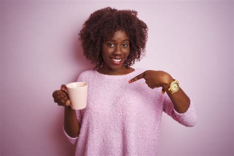 자신에게 손가락을 가리키는 깜짝 얼굴과 고립 된 분홍색 배경 위에 서있는 커피 잔을 들고있는 젊은 아프리카 아프로 여성 가리키기에 대한 스톡 사진 및 기타 이미지 Istock