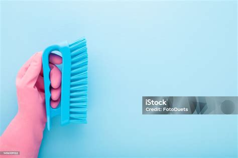 분홍색 고무 보호 장갑을 끼고 밝은 파란색 테이블 배경에 새 청소 브러시를 보여주는 깨끗한 손 파스텔 색상 근접 촬영 텍스트를 위한 빈 공간입니다 하향식 보기 가사 집안일에