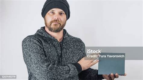 니트 모자를 쓴 흰색 배경에 수염이 있는 힙스터 남자가 광고를 위해 빈 회색 판지 표지판을 손에 들고 있습니다 공간을 복사합니다