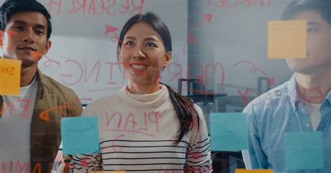 아시아 사업가들은 투명한 유리 벽 뒤에 서서 진행 상황을 가리키는 관리자의 말을 듣고 회의를 브레인스토밍하고 작업자는 사무실 벽에 스티커 메모를 게시합니다 비즈니스 영감