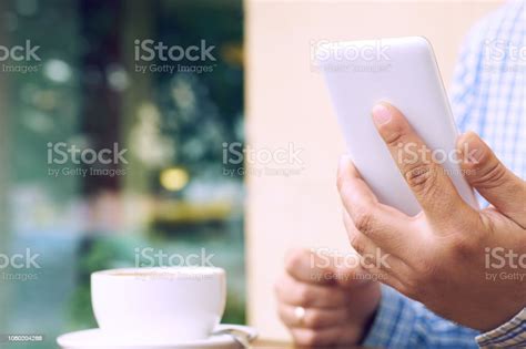 자른 이미지 젊은 남자 커피와 스마트 폰의 컵과 테이블에 앉아 전화에 메시지를 입력 하는 남자의 손을 터치 스크린 발코니 테라스에 앉아있는 동안 Brand Name