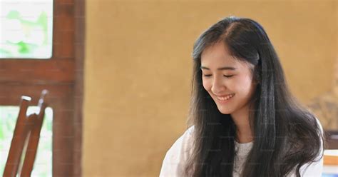 컴퓨터 노트북으로 작업하는 매력적인 아시아 여성의 사진은 빈티지 거실을 배경으로 커피 컵과 노트북 더미로 둘러싸인 나무 작업 책상에 올려 놓았습니다 사진