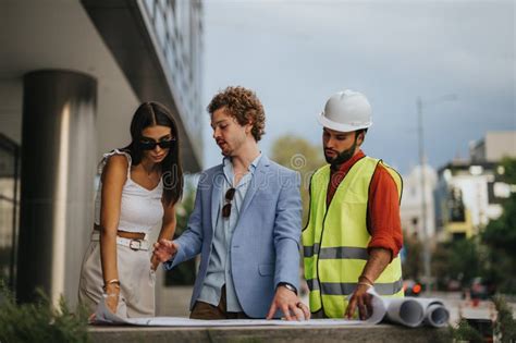 Architects And Engineers Discussing An Architectural Blueprint Outdoors Collaborating On A