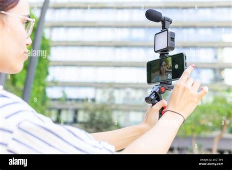 A Young Woman Captures Content Using A Smartphone Mounted On A Handheld Gimbal Outside A Modern
