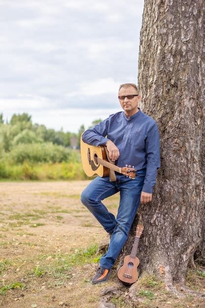Premium Photo A Man With A Guitar Leaning Against A Tree