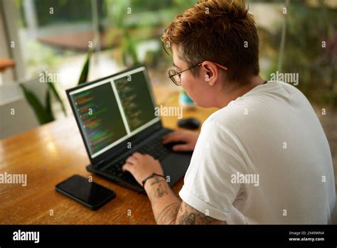 transgender web developer works on laptop programming in modern eco
