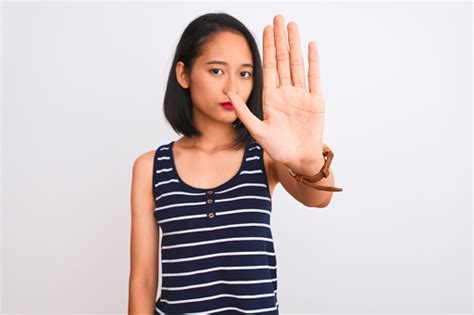 줄무늬 티셔츠를 입은 젊은 중국 여성이 고립된 흰색 배경 위에 서서 손바닥으로 노래를 멈추고 있습니다 얼굴에 부정적이고 심각한 제스처로 경고 표현 T 셔츠에 대한 스톡 사진