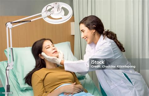 흰 가운을 입고 의료용 장갑을 낀 의사가 젊은 아시아 여성의 얼굴 피부를 검사하며 안면거상술 전에 준비한다 병원 클리닉의 미용 외과 분위기 알레르기 전문의에 대한 스톡 사진