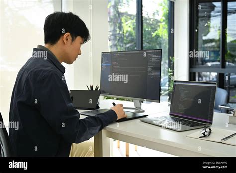 side view of male programmer sitting front of computers with coded data