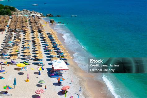 우산과 일광욕 의자가 있는 아름다운 깨끗한 모래와 자갈 해변에서 휴가를 보내는 사람들 햇볕이 잘 드는 산 푸른 해변 풍경 히마레 알바니아 Albanian Riviera에