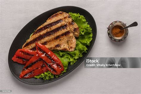 구운 고추와 양상추 잎을 밝은 린넨 배경의 검은 접시에 구운 칠면조 유방 스테이크 고추 셰이커 옆에 고추를 뿌립니다 맨 위 보기 복사 공간 0명에 대한 스톡 사진 및 기타