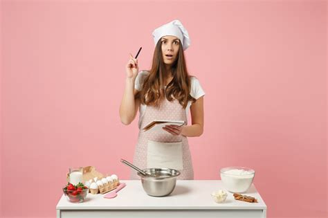 주부 요리사 요리 제과 또는 베이커 앞치마 흰색 티셔츠 모자 요리사 모자는 독창성과 스튜디오에서 분홍색 파스텔 배경에 고립 된