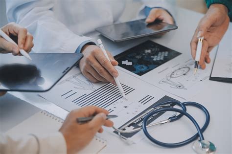 흰색 실험복을 입고 수술용 수술복을 입은 의사들이 테이블에 앉아 환자 기록에 대해 논의하는 다인종 의료진 간호사에 대한 스톡 사진 및 기타 이미지 Istock