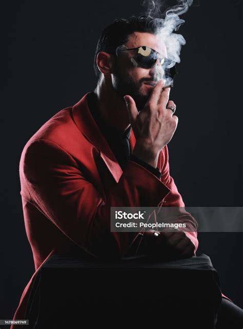 패션 흡연 빨간색은 어두운 배경에 스튜디오에서 남자 모델이 스타일을 위해 정장을 입고 있습니다 연기 마피아 담배를 들고 검은 공간에서 포즈를 취하는 잘생긴 젊은 남성과 함께
