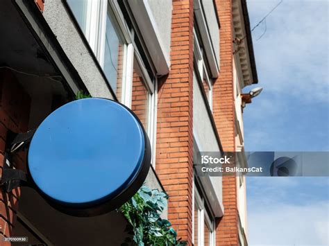 건물 외관에 매달려 있는 빈 파란색 원형 상점 간판은 유럽 도시 거리의 맑은 하늘을 배경으로 볼 수 있으며 소매업 광고 및 도시