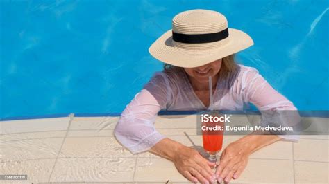 밀짚 모자를 쓴 금발 의 여인이 화창한 여름날 수영장 근처에서 휴식을 취하고 오렌지 칵테일을 마십니다 여름 무드 컨셉 휴가 모든 포함 가냘픈에 대한 스톡 사진 및 기타