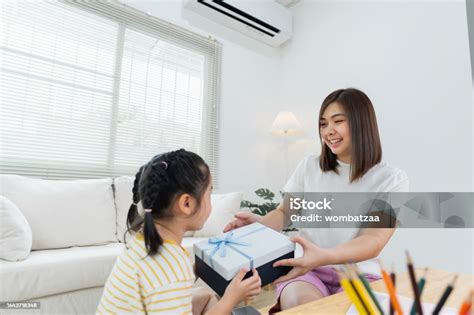 엄마에게 어머니의 날 선물을 주는 파란 선물 상자를 들고 있는 고마운 아시아 소녀 행복한 엄마와 귀여운 딸 아이가 생일을 축하하고 집에서 소파 소파에 껴안고 있다 행복한