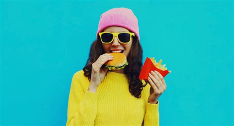 파란 화려한 배경에 햄버거와 감자 튀김 패스트 푸드를 먹는 세련된 행복 미소 젊은 여성의 초상화 20 29세에 대한 스톡 사진 및 기타 이미지 Istock