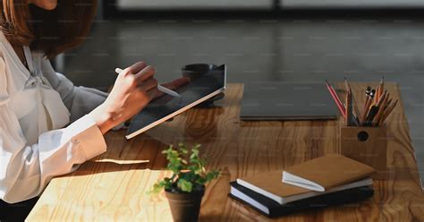 편안한 거실을 배경으로 하는 현대적인 나무 테이블에서 컴퓨터 노트북과 커피 컵 앞에서 스타일러스 펜과 태블릿을 손에 들고 있는