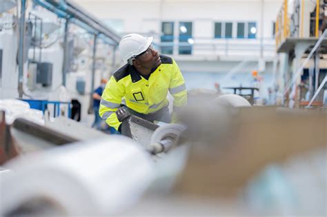 아프리카 남성 엔지니어 아래를 내려다보고 바퀴 만드는 기계를 검사합니다 헬멧과 조끼를 착용하십시오 대형 플라스틱 및 철강 제조 공장의 사업에 종사하고 있습니다 30 34세에