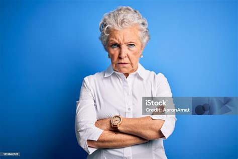 고립 된 파란색 배경 에 서 우아한 셔츠를 입고 선임 아름다운 여성은 교차 팔로 얼굴에 표정 회의적이고 긴장 거부 부정적인 사람 불쾌한에 대한 스톡 사진 및 기타 이미지