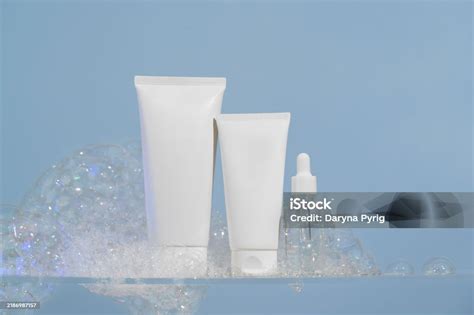 얼굴 또는 바디 크림의 흰색 모형 튜브와 거품 거품이 있는 파란색 고립된 배경에 있는 혈청 항아리 피부 정화 및 보습의 개념 매일 미용 용품 디자인을 위한 이미지 파란색에