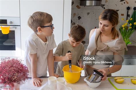 부엌에서 함께 빵을 굽고 있는 엄마와 아이들 어머니와 두 아들이 밝은 부엌에서 노란색 그릇에 재료를 섞고 밀가루를 체로 쳐서