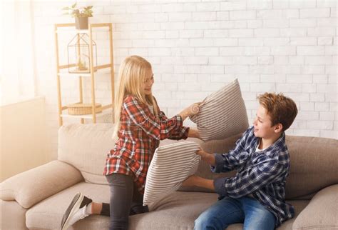 Happy Brother And Sister Having Pillow Fight On Couch Indoor Stock